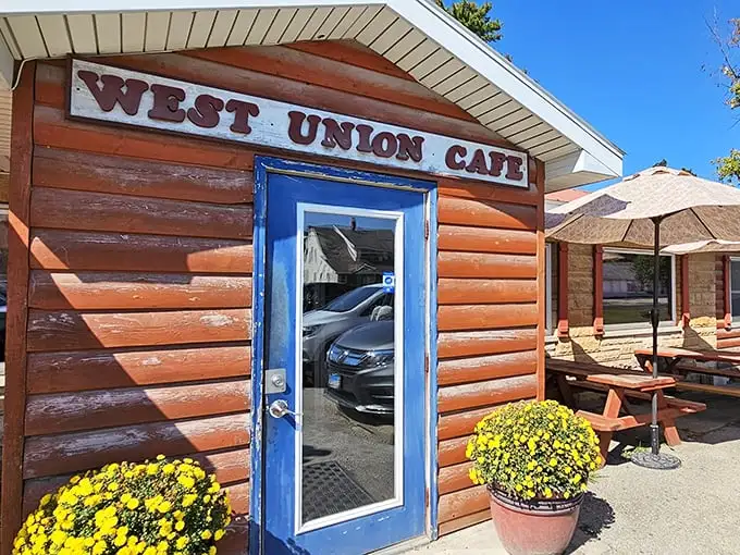The rustic log cabin exterior of West Union Cafe welcomes hungry travelers with its bright blue door and cheerful yellow mums—rural Illinois' version of a culinary red carpet.