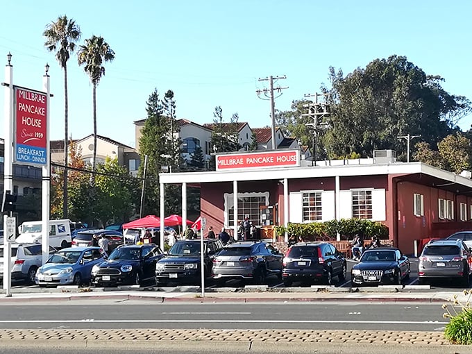 The iconic red exterior of Millbrae Pancake House stands like a beacon of breakfast hope, with cars parked out front as if everyone’s stopping by for pancakes.