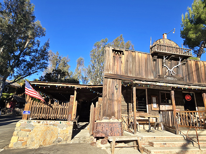 The weathered wooden facade of The Old Place stands proudly against blue skies, like a movie set where John Wayne might stroll in for dinner any minute.