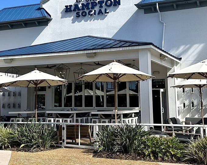 The Hampton Social's pristine white exterior with blue accents isn't just a building—it's a promise of coastal elegance waiting just beyond those doors.