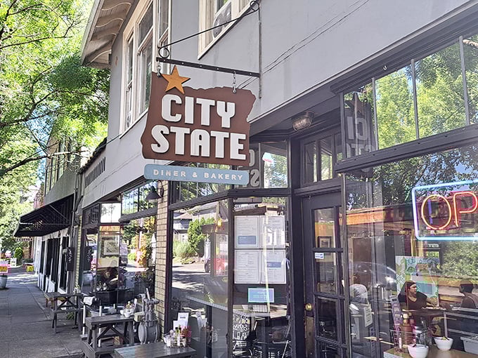The iconic Oregon-shaped sign welcomes hungry pilgrims to City State Diner & Bakery, where Portland's breakfast dreams come true beneath those towering trees.