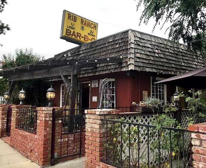 The rustic red exterior of Rib Ranch BBQ stands like a time capsule from the Old West, complete with wooden shingles and that iconic yellow sign beckoning hungry travelers.