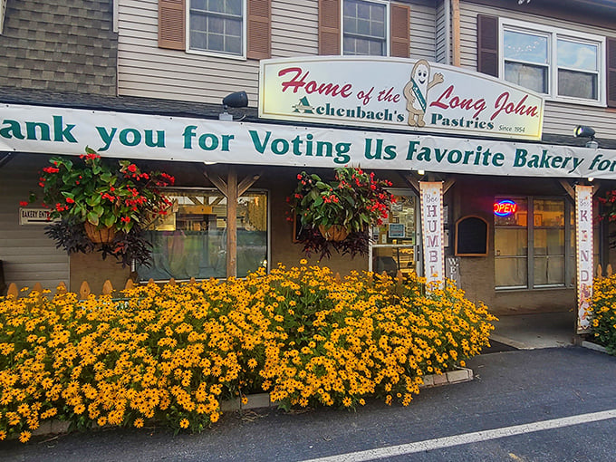 The welcoming facade of Achenbach's, where vibrant marigolds and hanging baskets frame a bakery that's earned its "favorite" status through decades of pastry perfection.