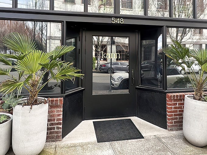 Kann's sleek exterior beckons with tropical palm sentinels standing guard. The modern black façade with "548" prominently displayed offers a stylish Portland welcome.