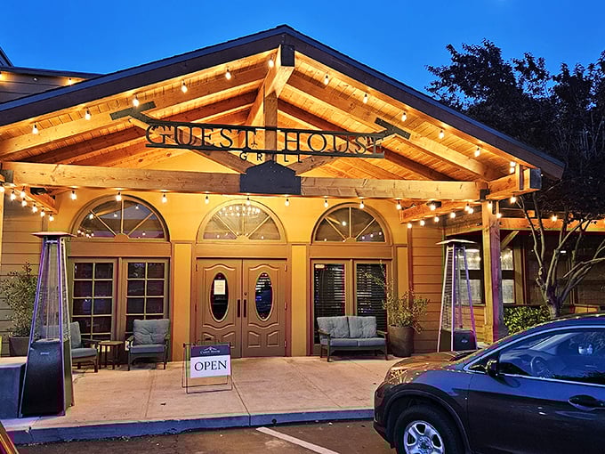 The warm glow of Guest House Grill's exterior beckons like a lighthouse for hungry travelers. String lights twinkle against wooden beams, promising comfort within.