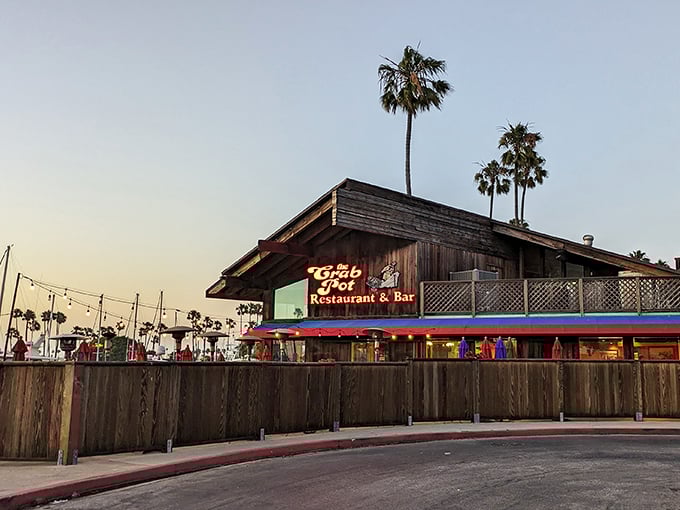 Sunset casts a golden glow on The Crab Pot, where string lights twinkle like stars and the promise of ocean-fresh delicacies awaits beneath that rustic roof.