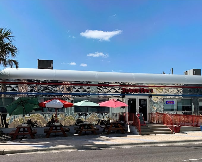The gleaming silver exterior of Starlite Diner catches Florida sunshine like a time machine from the 1950s, complete with palm trees and red umbrellas for that perfect retro vibe.