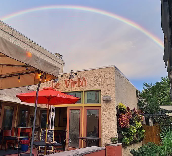 A rainbow arches over Le Virtù's stone façade like nature's own stamp of approval. The red umbrellas and lush greenery create an inviting oasis in South Philly.
