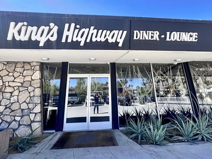 The iconic King's Highway sign welcomes desert travelers like a mid-century mirage, promising culinary salvation behind those stone-faced walls and gleaming glass doors.
