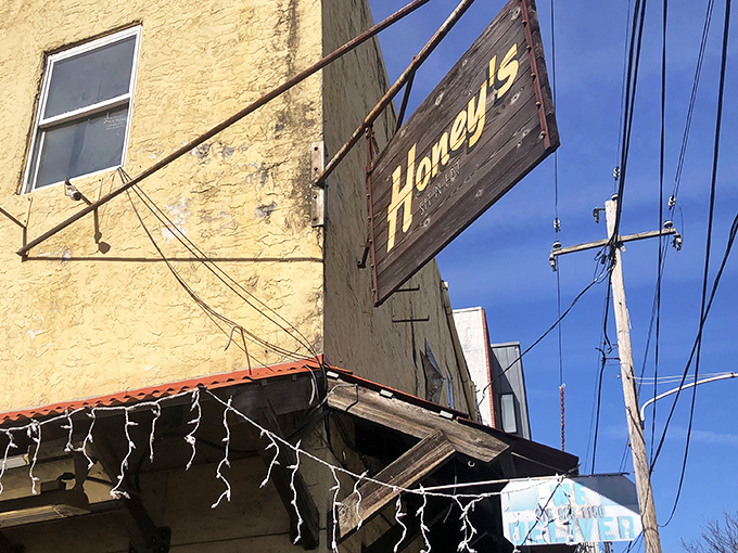 The weathered wooden sign against that mustard-yellow exterior says it all: unpretentious, welcoming, and promising something far better than its humble appearance suggests.