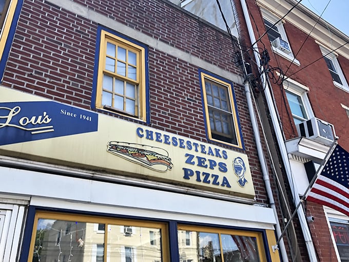 The vintage sign proudly announces Lou's specialties against the brick backdrop. That cartoon face knows something you don't—how good lunch is about to be.