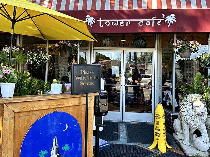 The welcoming entrance to Tower Café beckons with vibrant yellow umbrellas and lush greenery—like stepping into a tropical vacation right in Sacramento.