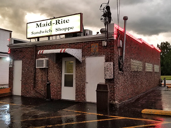 The humble brick exterior of Maid-Rite stands defiant against stormy skies, like a culinary lighthouse beckoning hungry travelers through the rain.