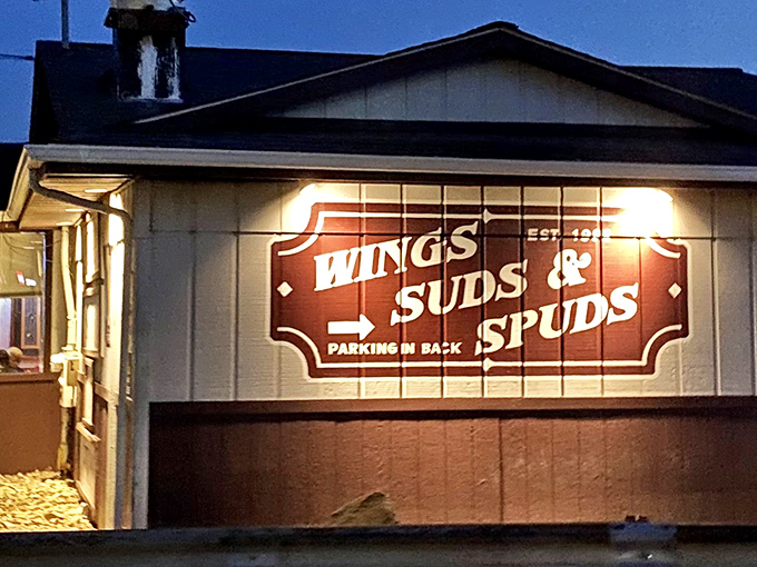 The illuminated sign glows like a beacon for wing lovers, promising three essential food groups: Wings, Suds & Spuds. Parking directions included!