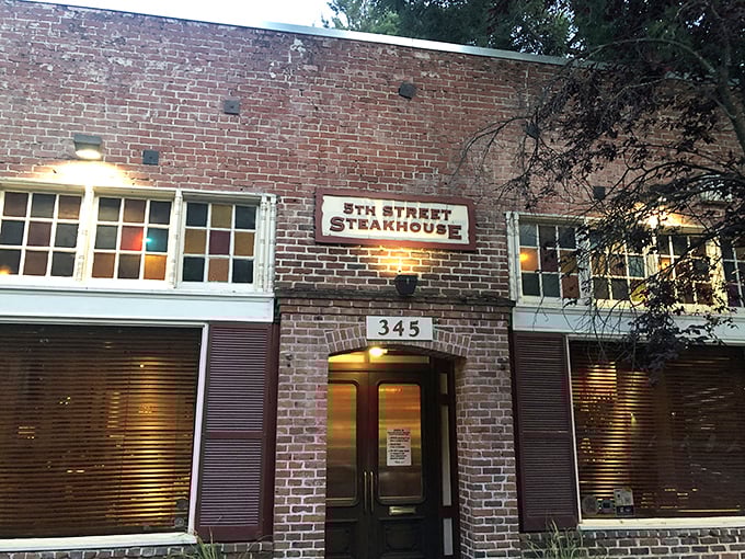 The brick facade of 5th Street Steakhouse stands like a sentinel of sizzle, promising carnivorous delights behind those colorful stained-glass windows.