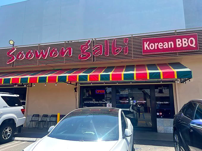The vibrant red sign of Soowon Galbi beckons like a culinary lighthouse in Koreatown, promising charcoal-kissed delights beneath that cheerful striped awning.