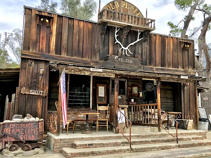 The weathered wooden facade of The Old Place stands proudly against blue skies, like a movie set where John Wayne might stroll in for dinner any minute.
