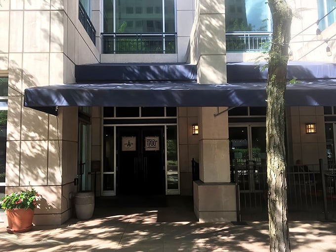 Dappled sunlight plays across the elegant entrance, where a navy awning offers shade and a hint of the sophisticated experience awaiting inside.