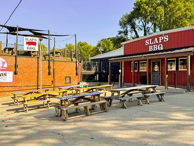 The bright red exterior of Slap's BBQ stands like a beacon of smoky promise, with picnic tables awaiting the faithful who make the pilgrimage.