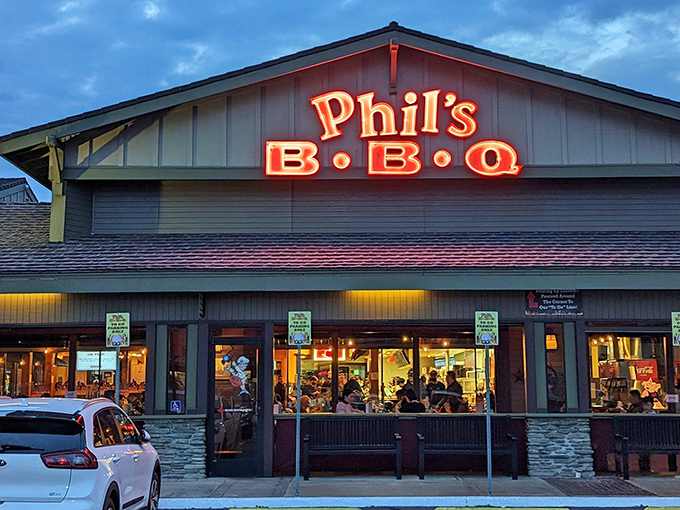 The neon glow of Phil's BBQ sign beckons hungry travelers like a barbecue lighthouse, promising smoky salvation after a long day.