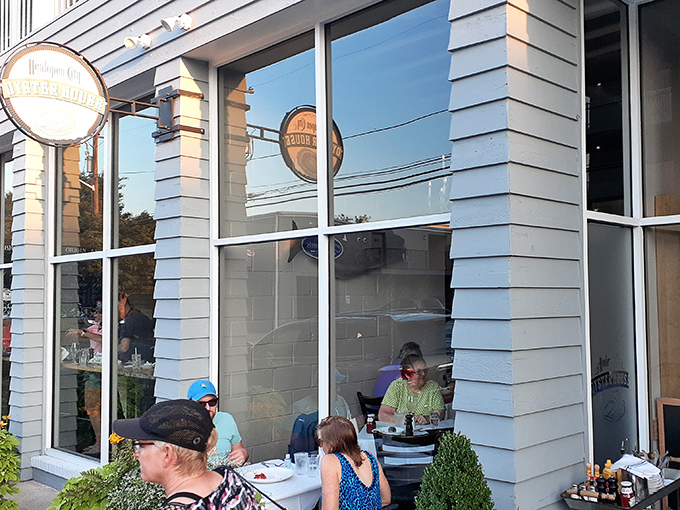 The blue-gray exterior of Henlopen City Oyster House beckons hungry passersby with its warm glow and lively atmosphere at dusk.