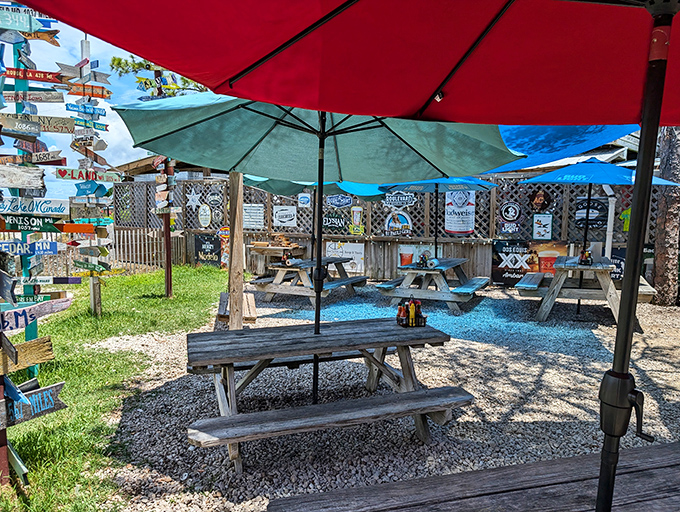 The weathered metal roof and "Sunny Place for Shady People" sign tell you everything you need to know—authenticity awaits beneath those red umbrellas.