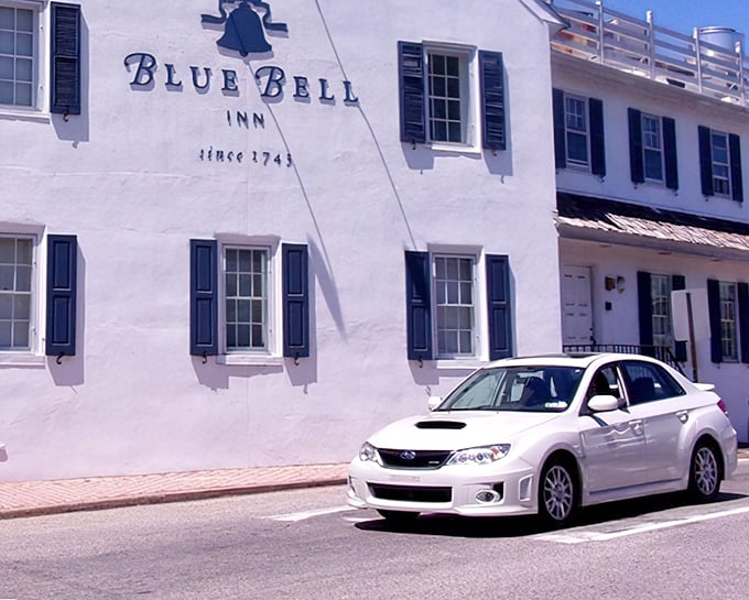 The historic Blue Bell Inn stands proudly in Pennsylvania sunshine, its whitewashed exterior and classic black shutters whispering stories from centuries past.