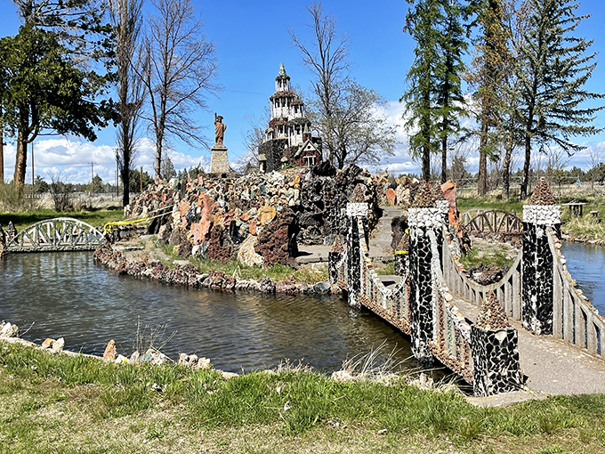 Where fantasy meets geology—a miniature stone castle and Statue of Liberty stand proudly beside a handcrafted bridge spanning peaceful waters.