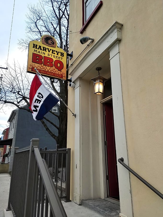 The unassuming entrance to Harvey's Main Street BBQ beckons with its vintage sign and "Open" flag – like a secret handshake for barbecue aficionados.