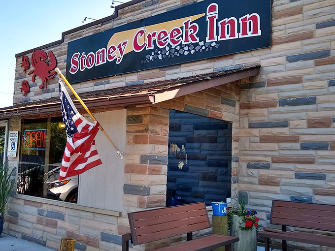 The stone facade of Stoney Creek Inn welcomes seafood pilgrims with its iconic red crab sign and American flag – Maryland hospitality in architectural form.