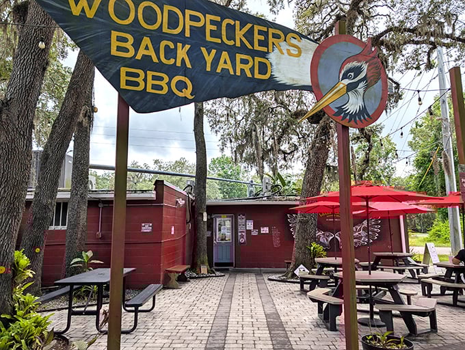 The entrance to barbecue paradise isn't always pearly gates – sometimes it's a rustic red building with a woodpecker sign promising smoky delights.