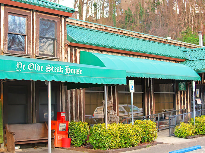 The iconic green awning and rustic log cabin exterior of Ye Olde Steak House stands as a beacon for carnivores seeking refuge from the ordinary.