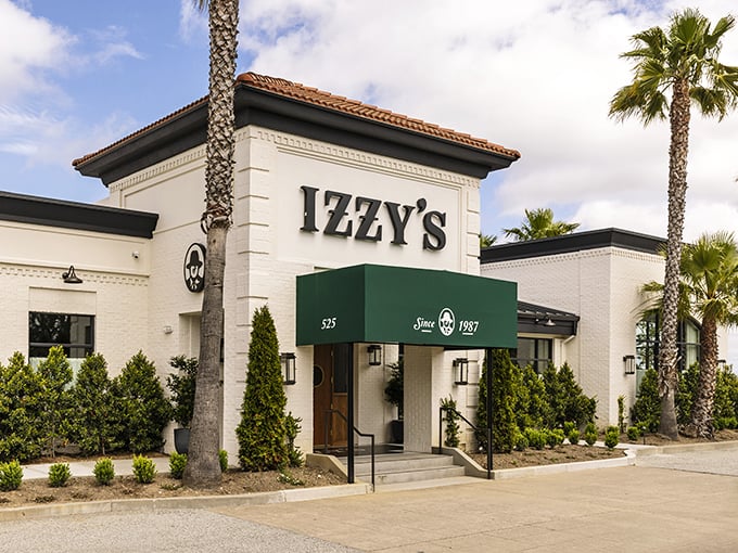 The iconic white exterior of Izzy's on the Peninsula stands like a beacon for carnivores, palm trees swaying as if applauding your excellent dinner choice.