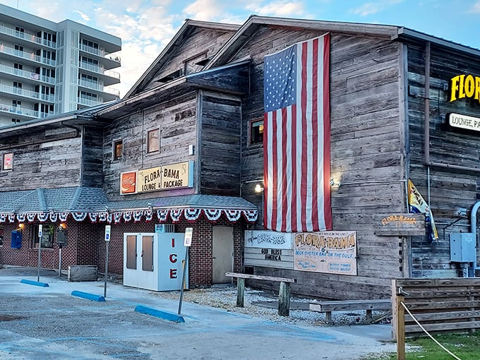 The weathered wooden exterior of Flora-Bama proudly displays its iconic yellow signage and American flag – a true Gulf Coast landmark straddling two states.