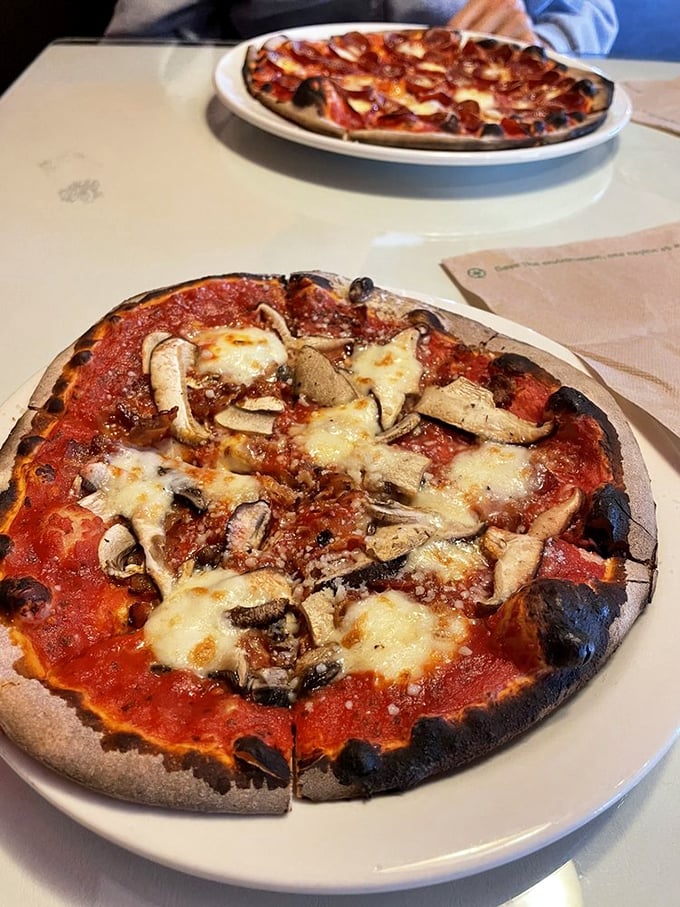 Two pizzas sharing a table like old friends catching up—one mushroom-laden, the other a mystery, both looking like they deserve your undivided attention.
