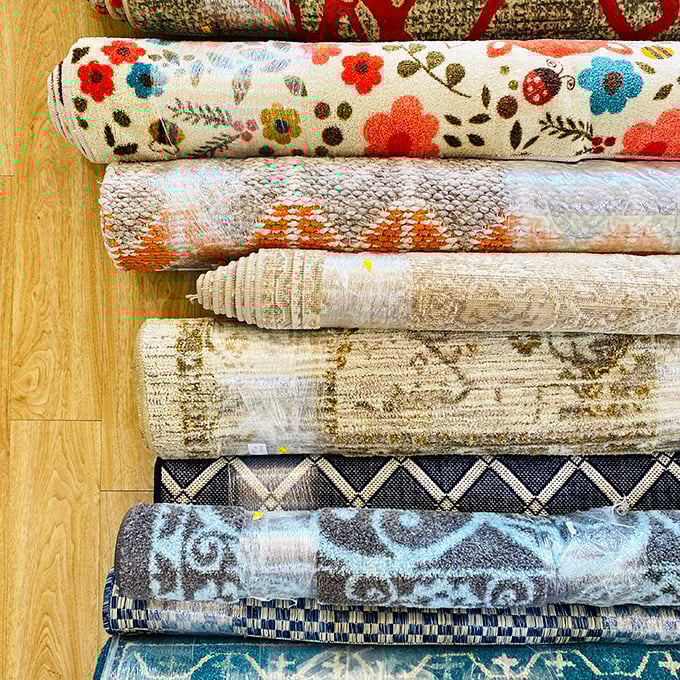 Rolled rugs tell stories of past lives while awaiting new floors to grace—each pattern a conversation starter for your next dinner party.