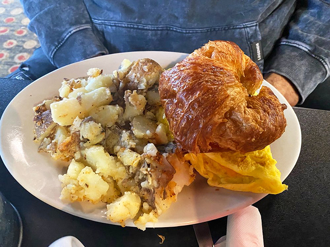 A breakfast sandwich on a buttery croissant with golden home fries—proof that mornings can indeed be wonderful.