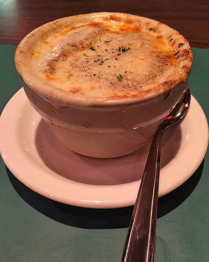 The French onion soup arrives like a sealed treasure chest – that golden, bubbling cheese top hiding the savory broth and tender onions below.