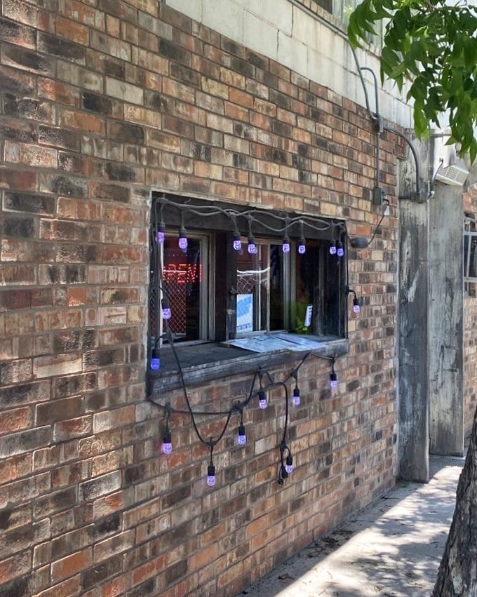 That humble order window, strung with purple lights, might as well be a portal to burger nirvana—the brick exterior hiding culinary treasures within.