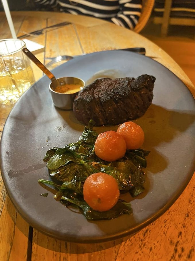 This steak doesn't just sit on the plate—it commands attention with a side of greens and roasted tomatoes that know their supporting role perfectly.