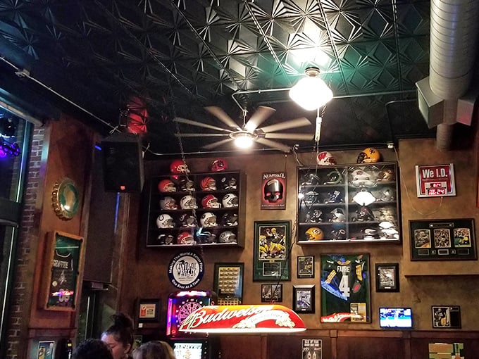 Football helmets line the walls like trophies in a museum of American sports culture, while the pressed tin ceiling adds vintage charm to every touchdown celebration.