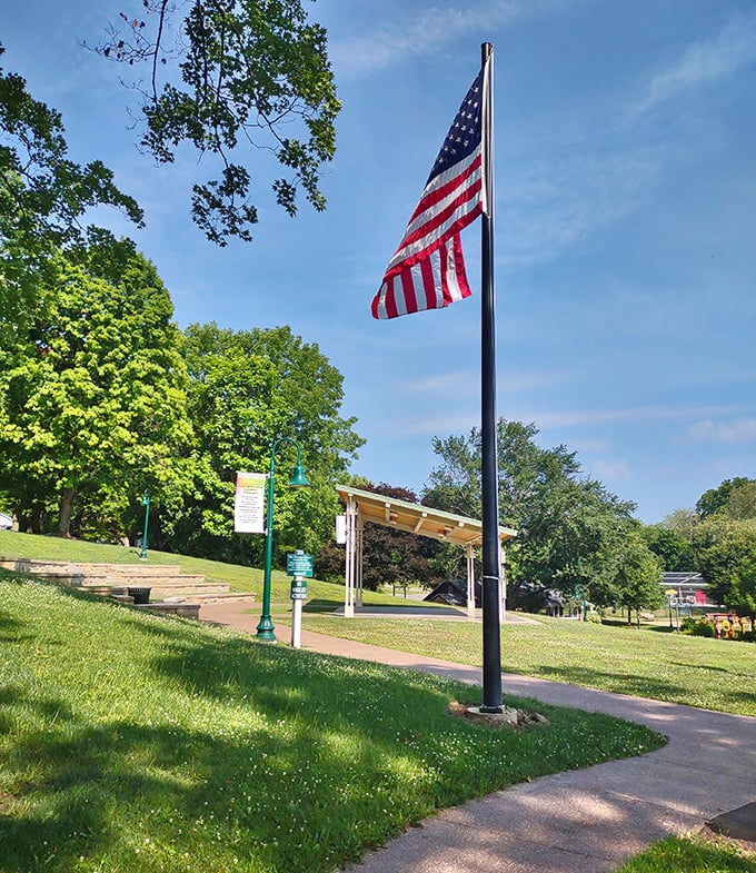 Old Glory stands tall in the borough park – a timeless symbol watching over generations of community picnics and first kisses.