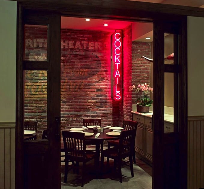 The "Cocktails" sign glows like a ruby beacon, promising liquid comfort in a room that feels like your coolest friend's dining room. 