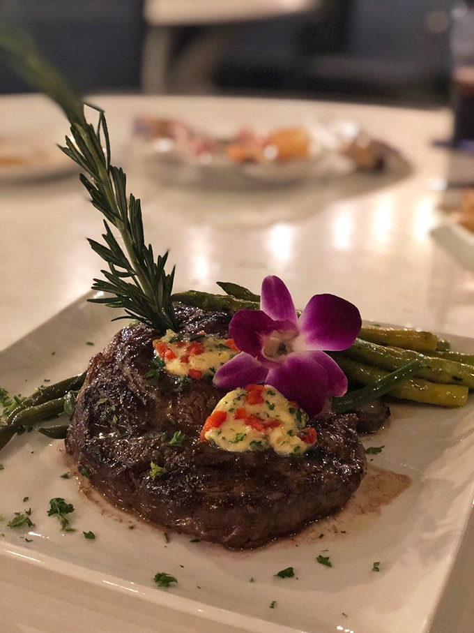 A perfectly seared ribeye adorned with herb butter and an edible flower – because even steakhouses get jealous of seafood joints sometimes.