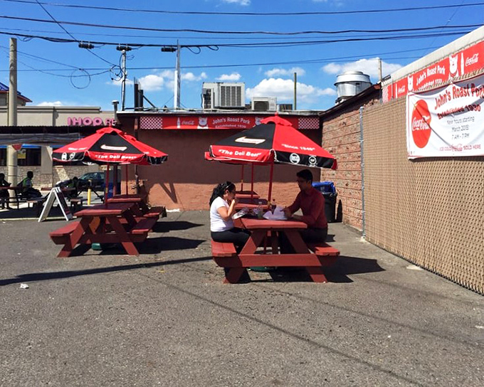 Red picnic tables under Coca-Cola umbrellas—where sandwich memories are made and diet plans go to die, gloriously and without regret.