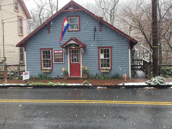 Even in winter's embrace, this little blue cottage stands defiant, its cheerful red trim a reminder that color exists even in monochrome seasons.
