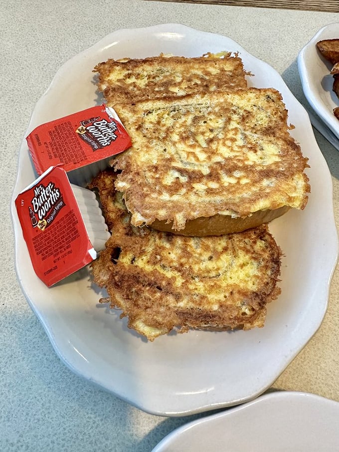 Golden-brown French toast that's achieved that mythical balance – crispy exterior giving way to custardy insides, with butter packets standing by for duty.