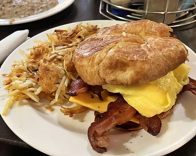 Breakfast engineering at its finest—golden croissant, melty cheese, and perfectly cooked eggs with a side of crispy hash browns.