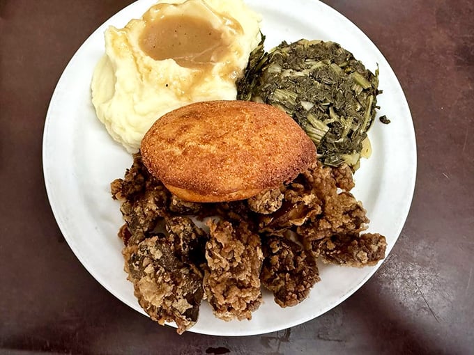 A classic Southern meat-and-three featuring mashed potatoes with gravy, collard greens, and a cornbread muffin—comfort food that speaks a universal language.
