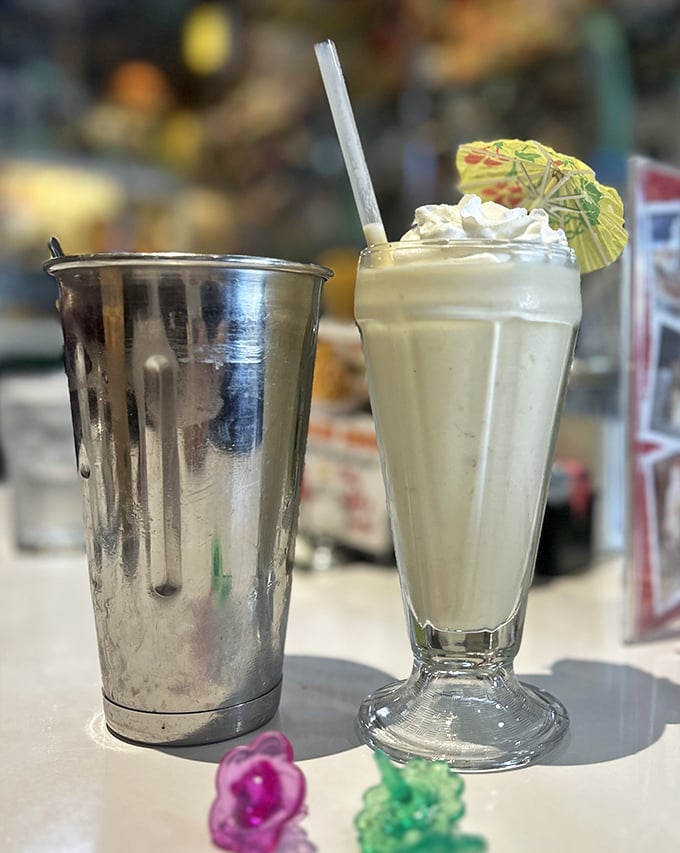 A proper milkshake served with the mixing tin—because one glass is never enough. That tiny umbrella isn't decoration, it's optimism.
